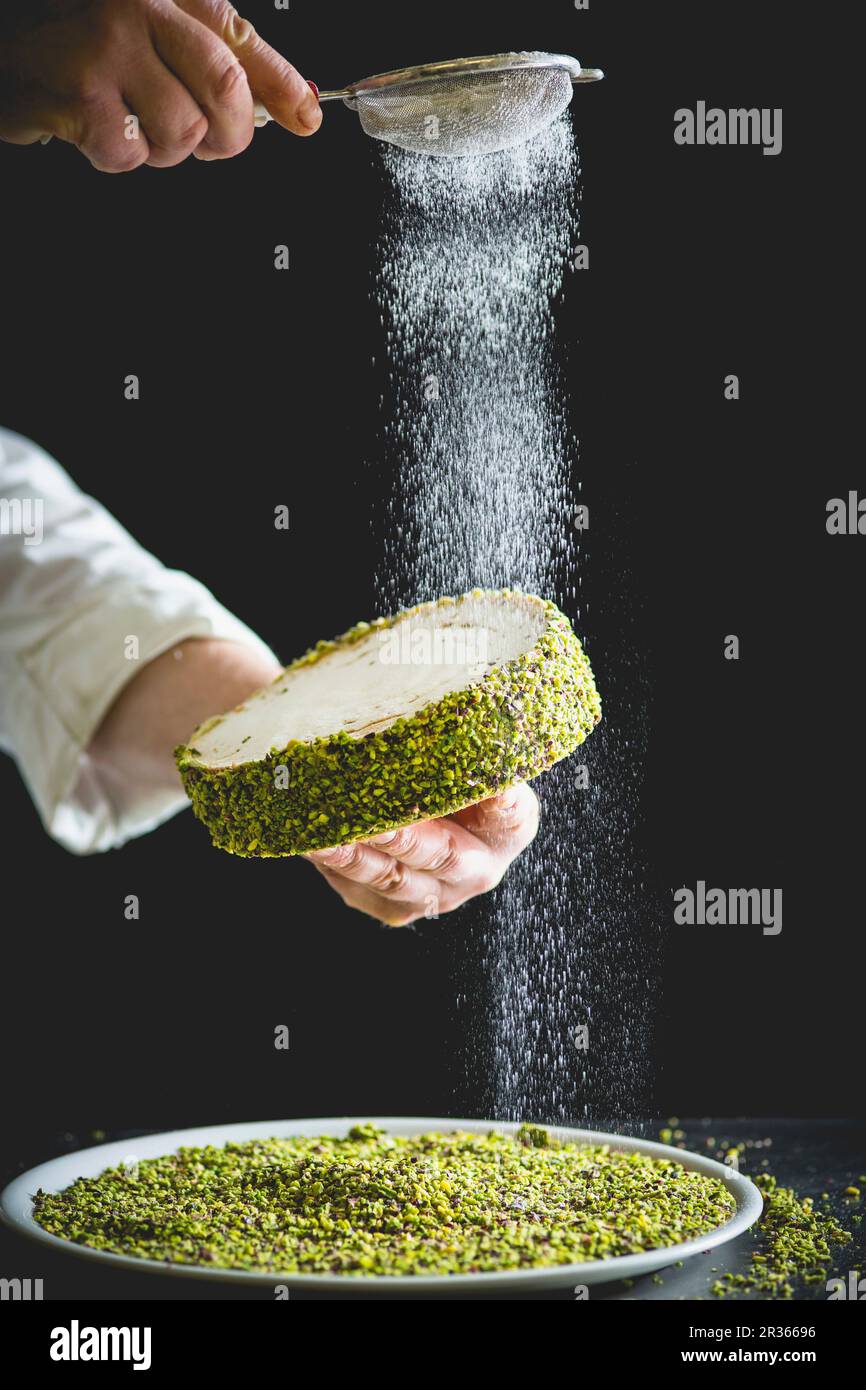 A confectioner dusting a small pistachio cake with icing sugar Stock ...