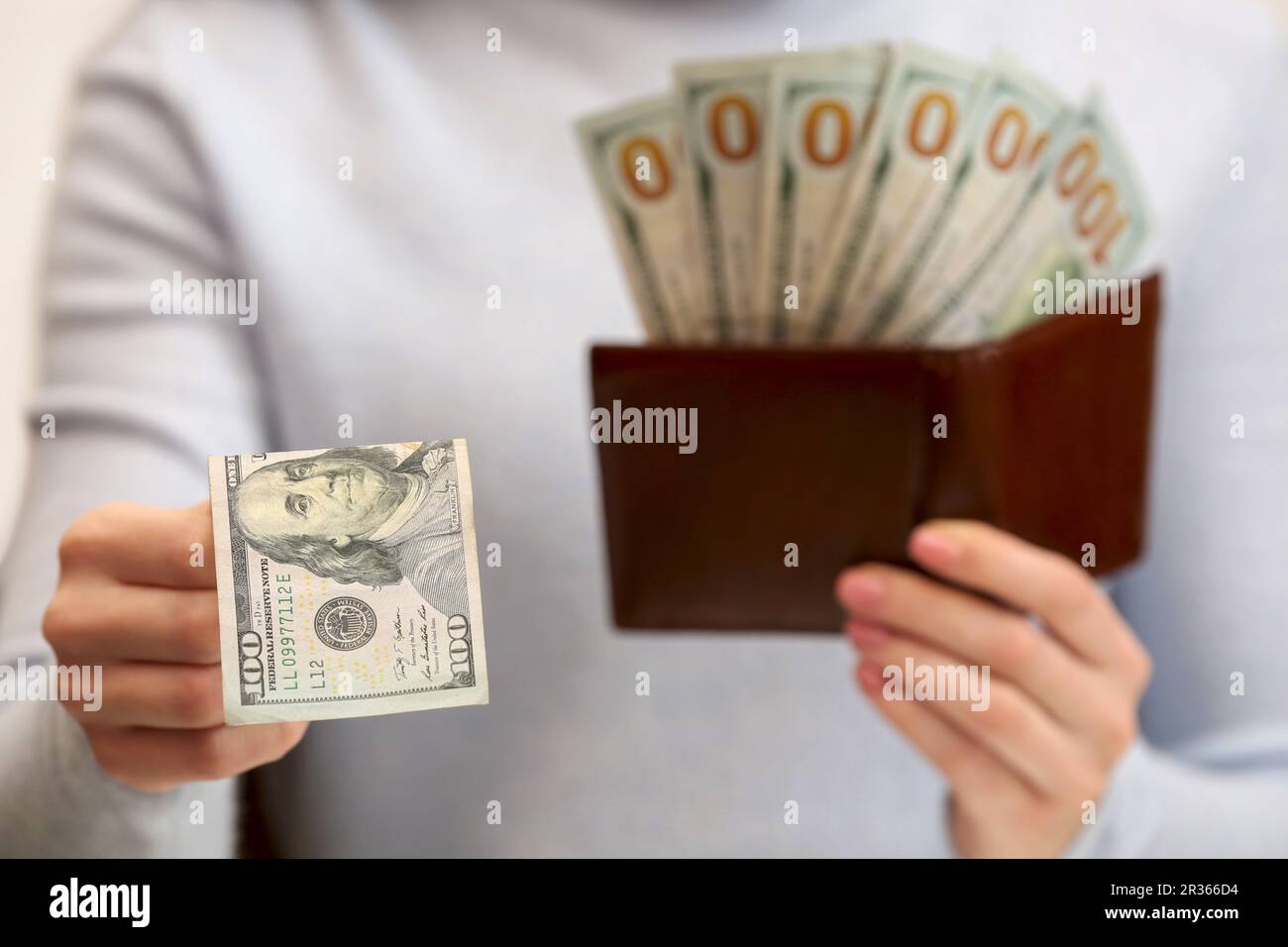 Woman giving 100 dollar bill and holding brown leather wallet with ...