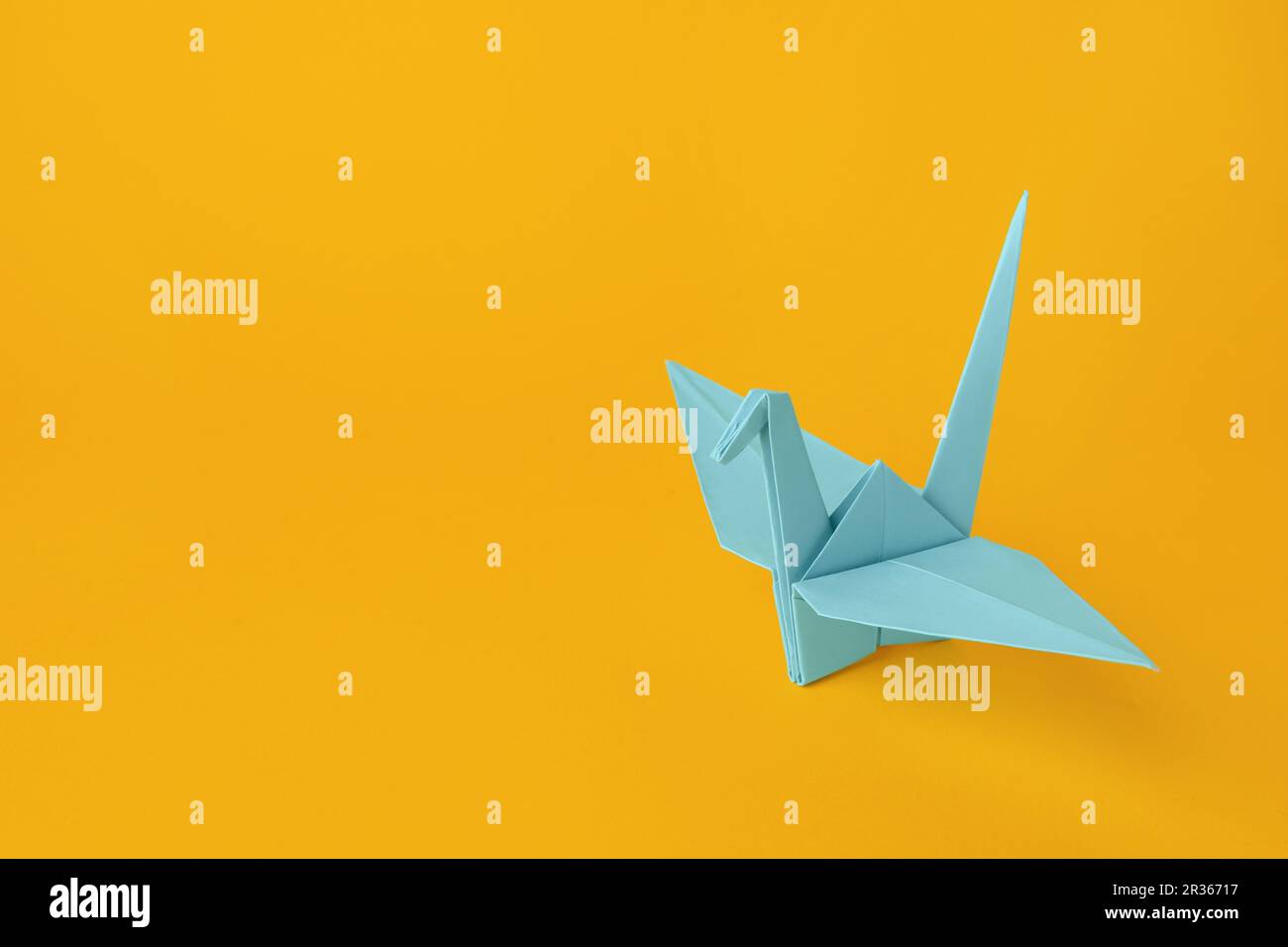 Origami art. Beautiful light blue paper crane on orange background ...