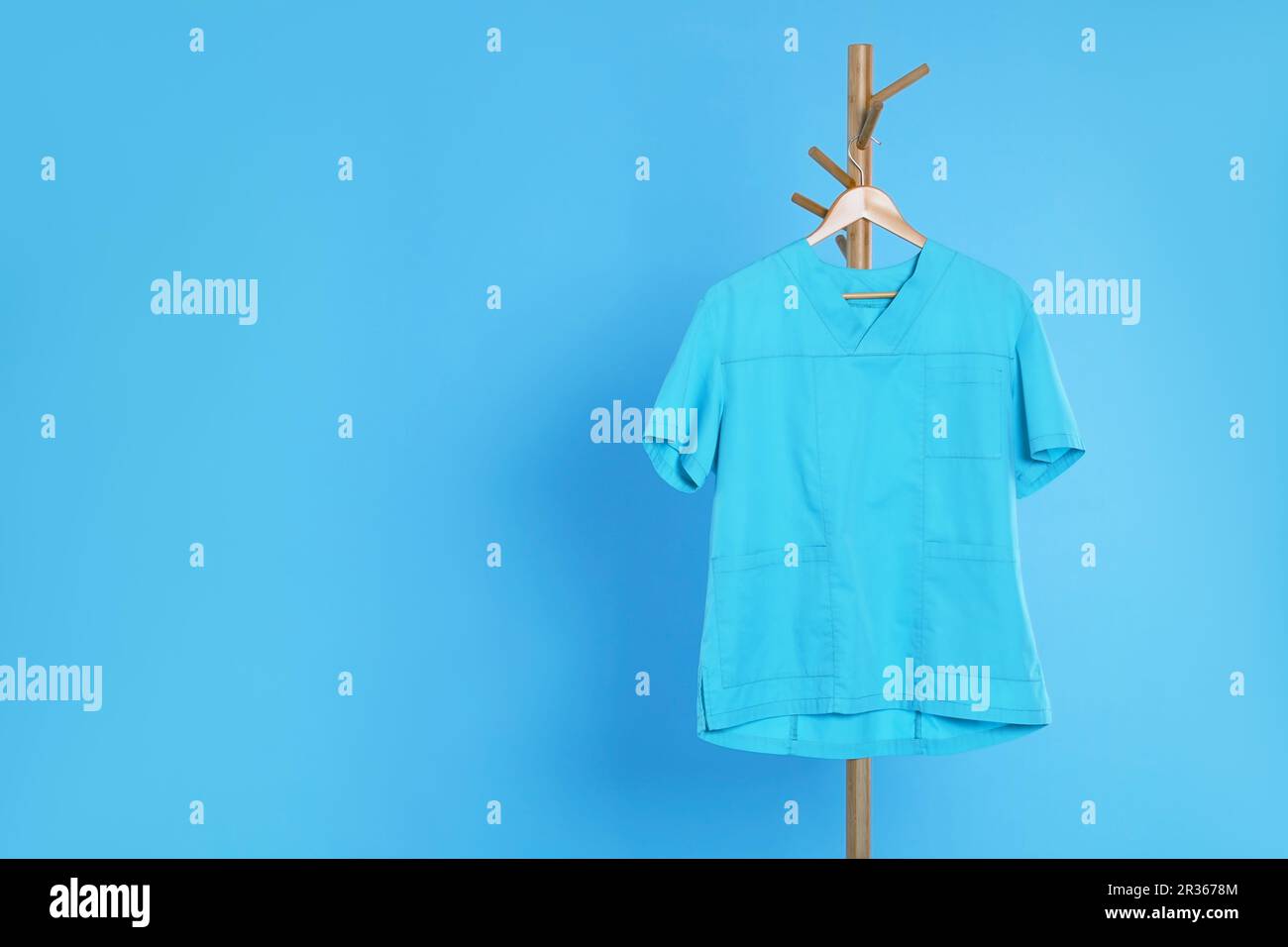 Turquoise medical uniform hanging on rack against light blue background ...