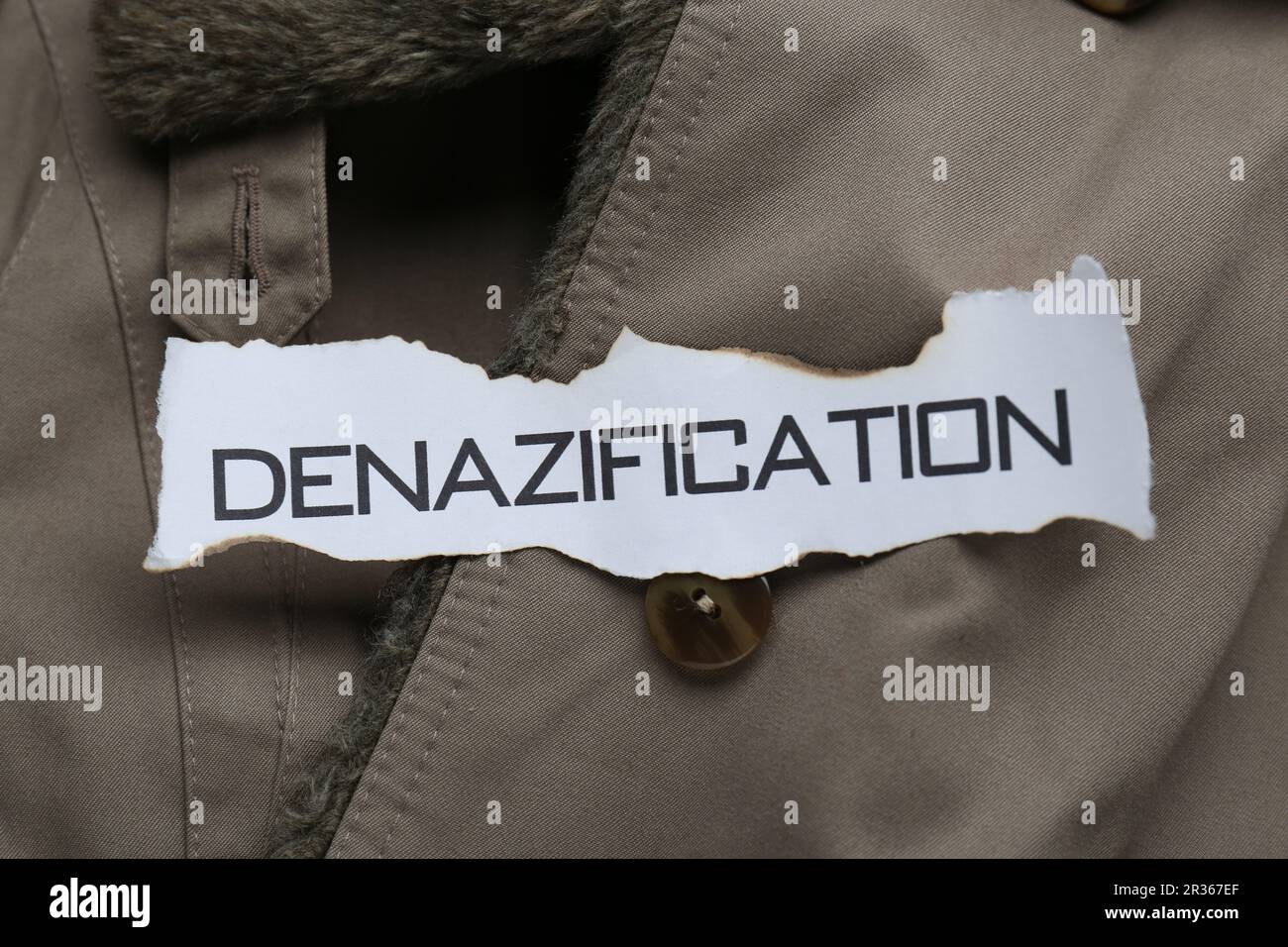 Piece of burnt paper with word Denazification on grey jacket, top view ...