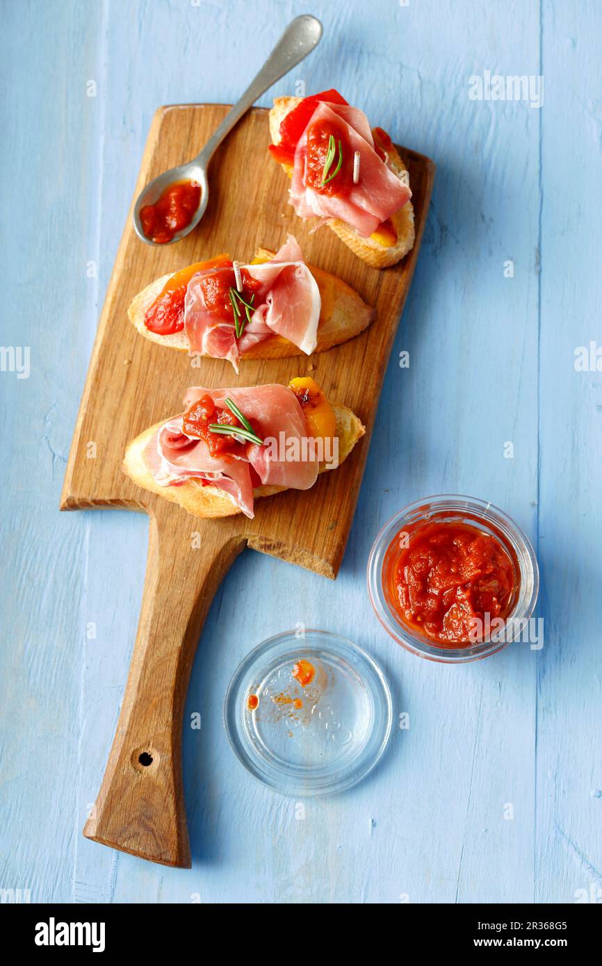 Sliced baguette topped with Serrano ham, grilled peppers and hot tomato ...