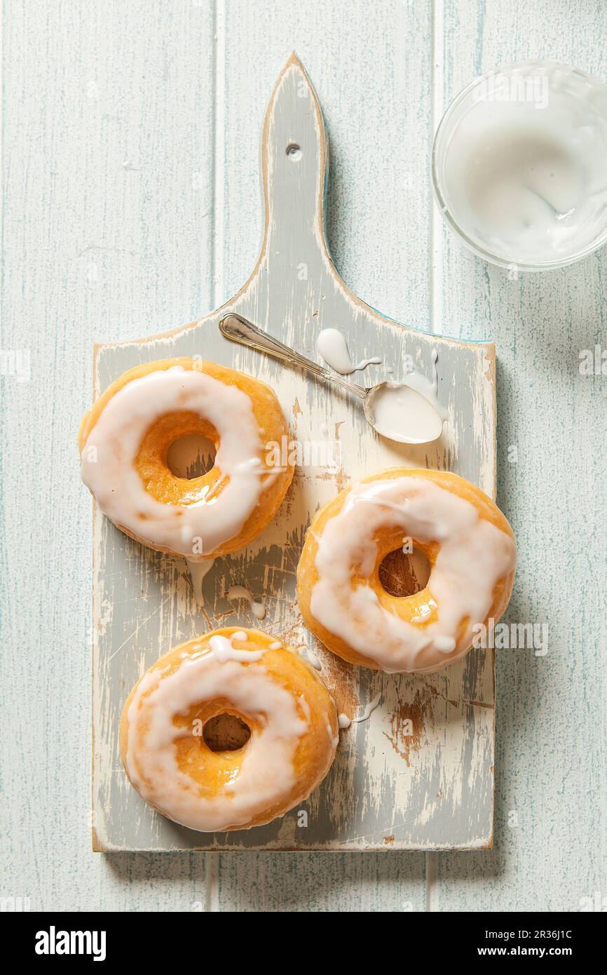 Three iced doughnuts on a grey wooden chopping board with a spoon Stock ...