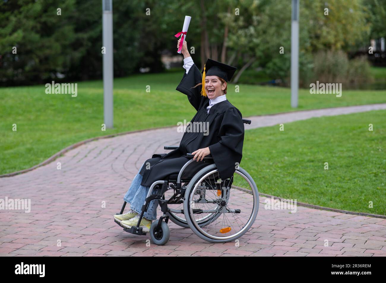 Caucasian woman in a wheelchair in a graduate costume rejoices at ...
