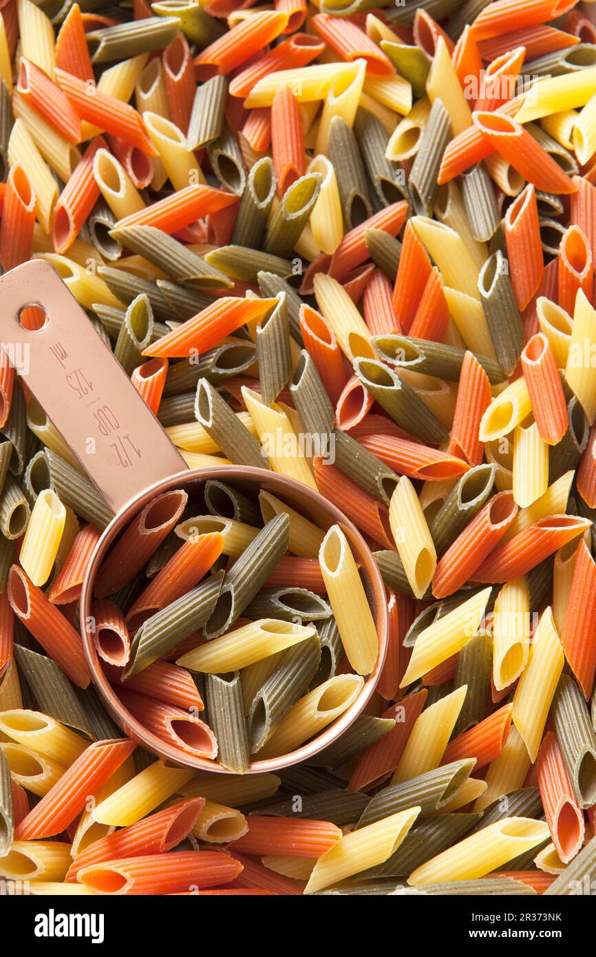 Tricolore penne pasta with a copper measuring cup Stock Photo - Alamy
