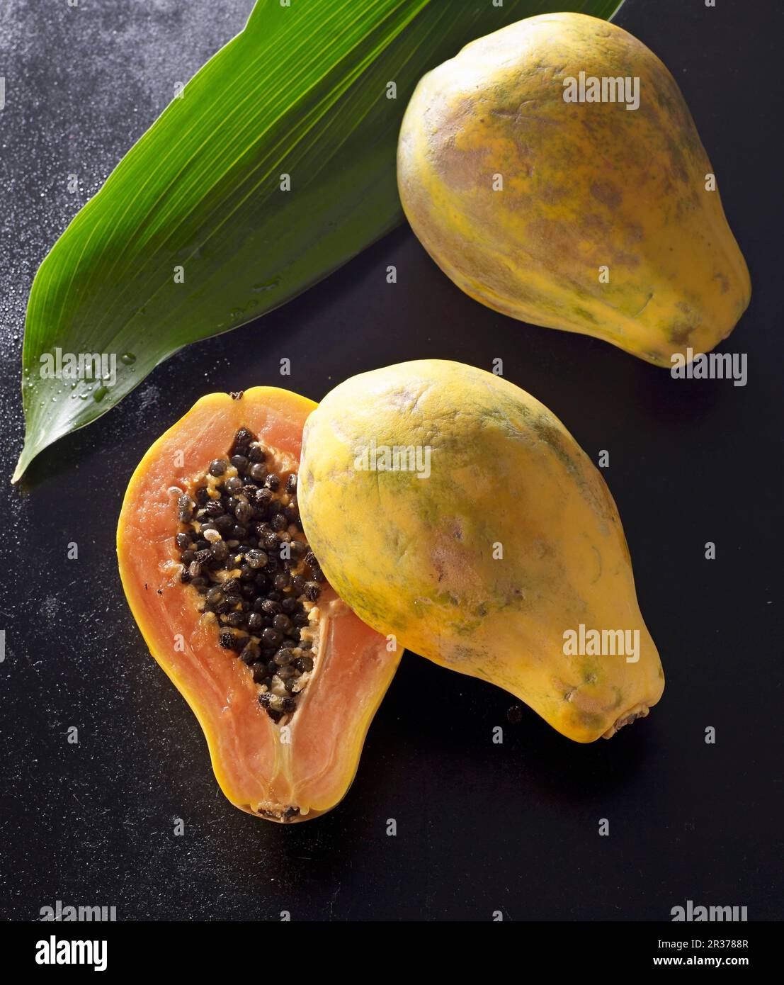 Two papayas, one halved, with a palm leaf Stock Photo - Alamy