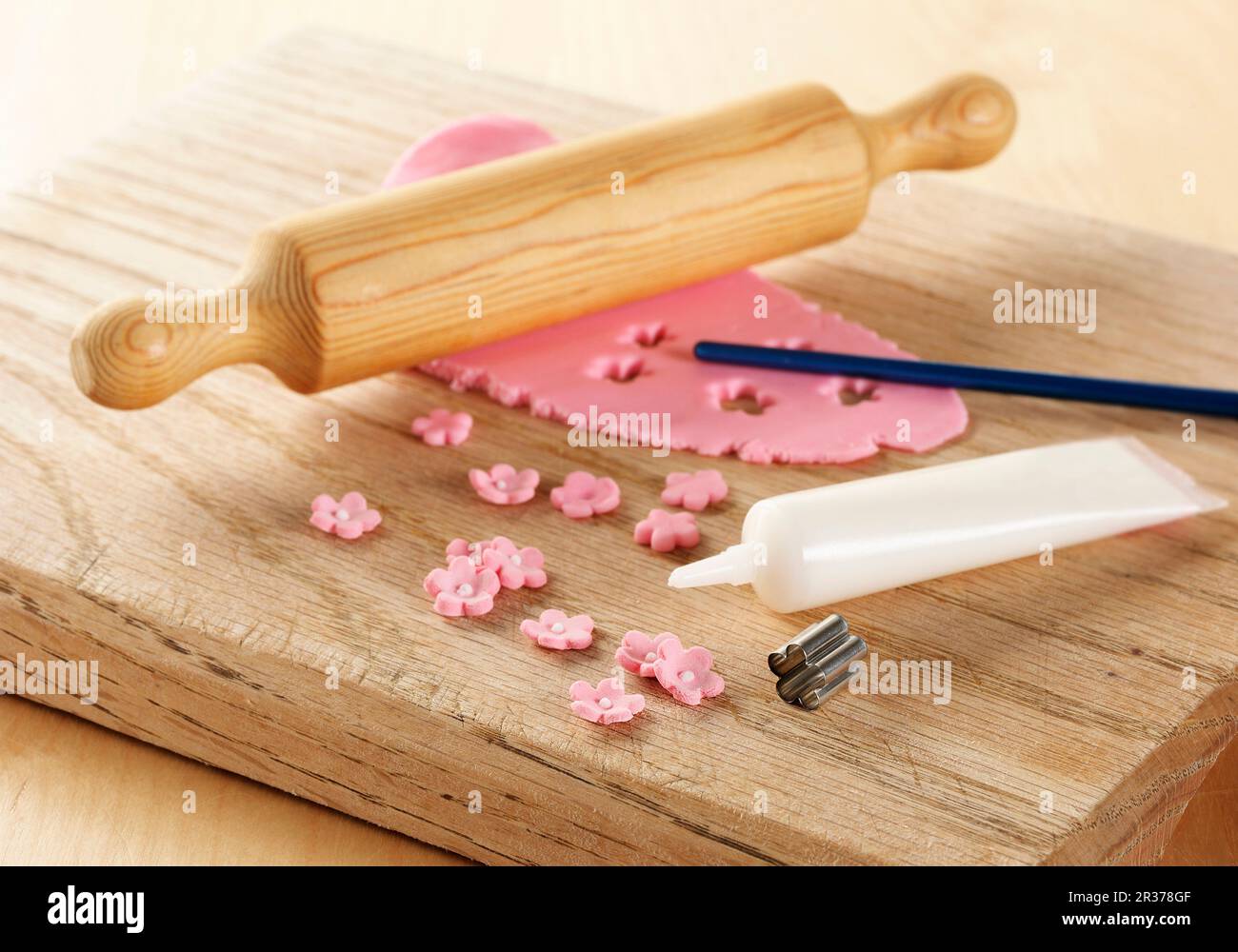Pink icing rolled out on a board with rolling pin, showing a metal ...