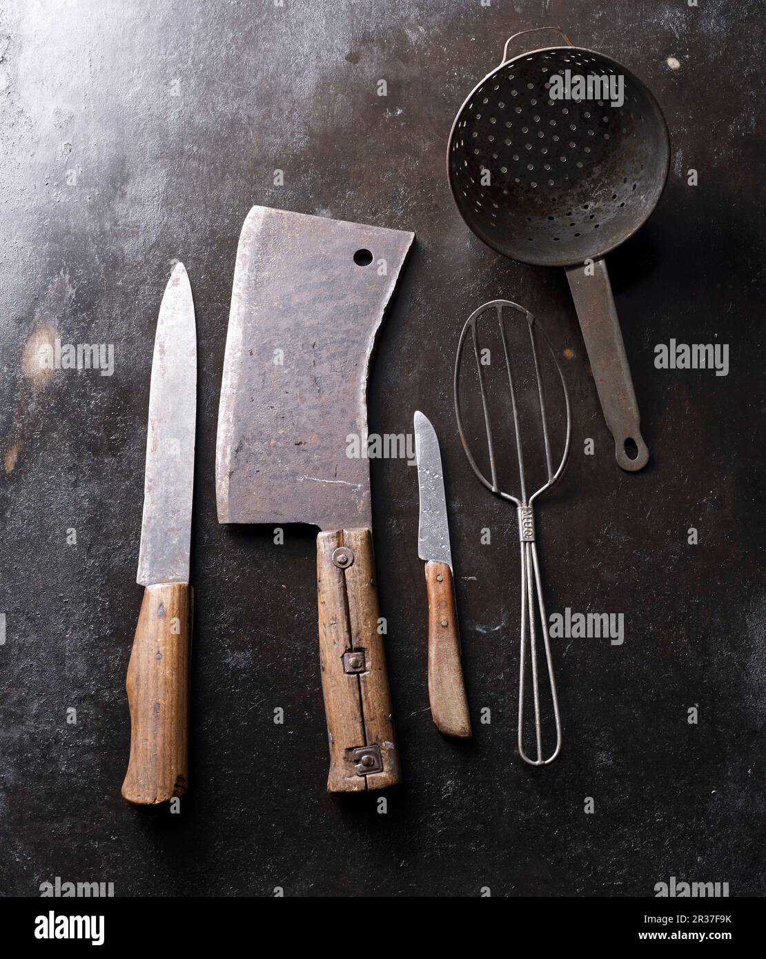 Old kitchen utensils on a dark background: meat cleaver, wire spoon ...