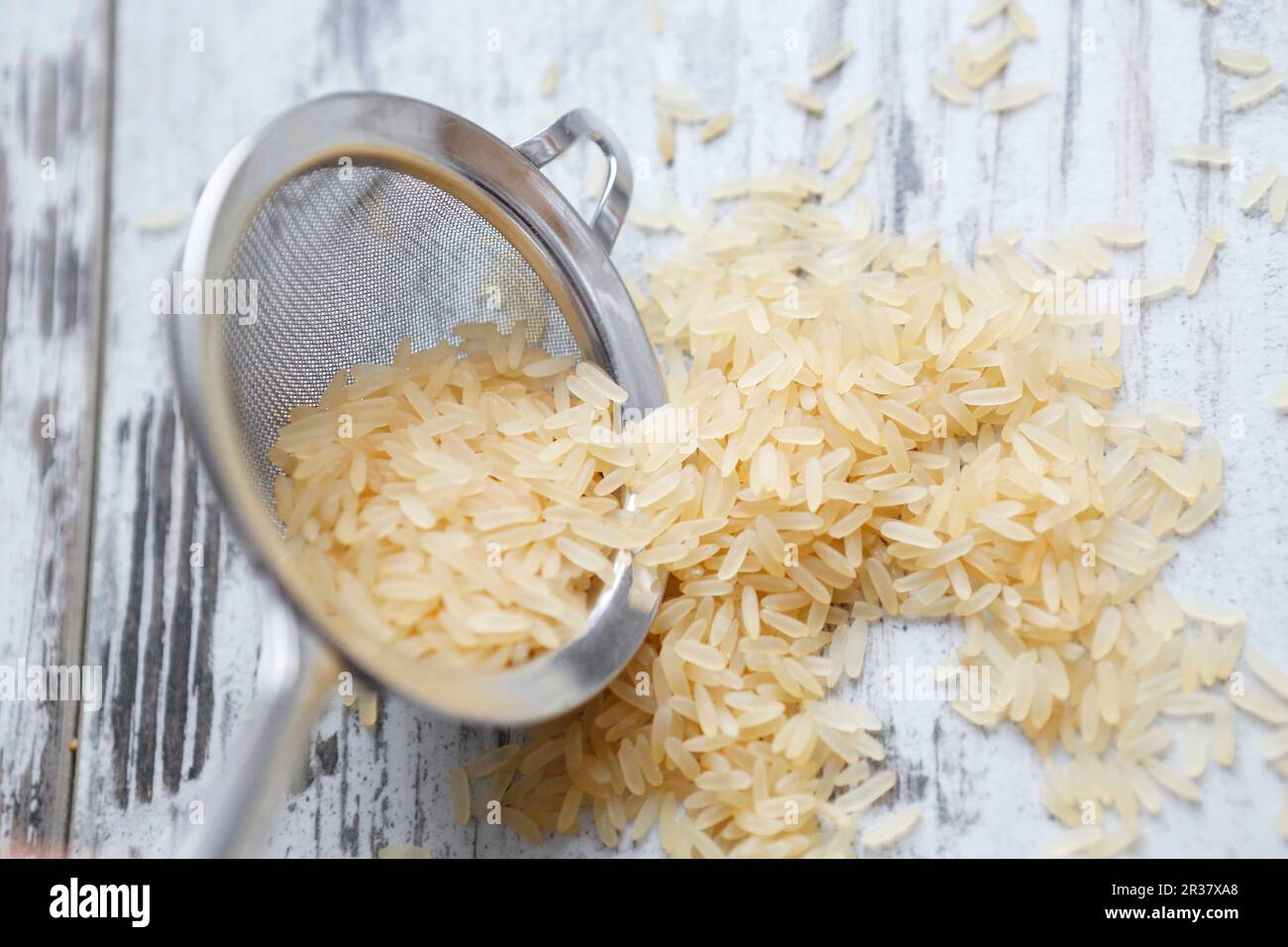 Long-grain rice in a sieve and on a wooden background Stock Photo - Alamy