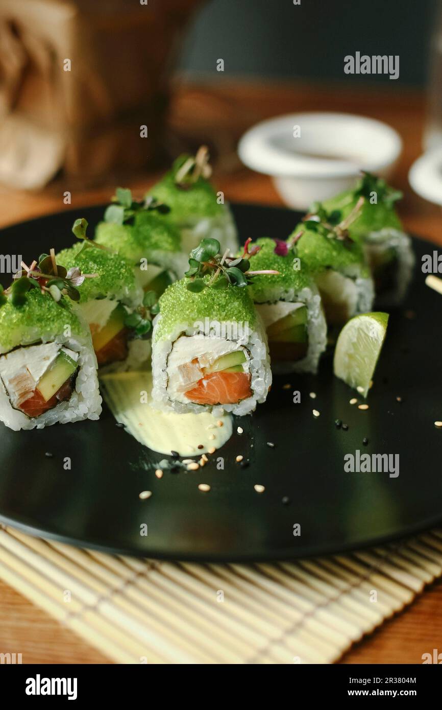 Sushi rolls with salmon, avocado, fresh cheese and green coloured fish ...