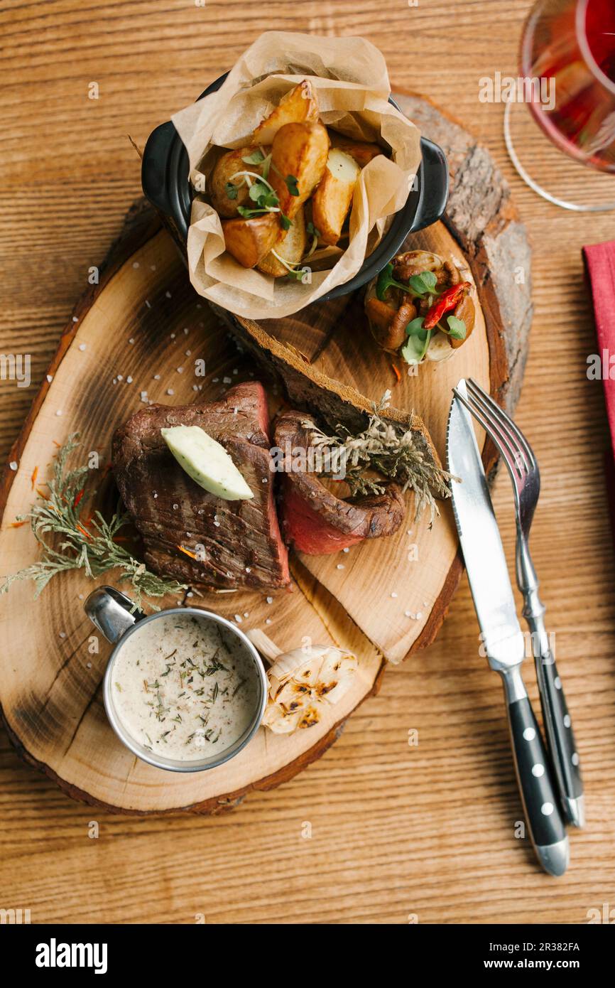 Steak with roasted potatoes and mushroom sauce served on a tree slab ...
