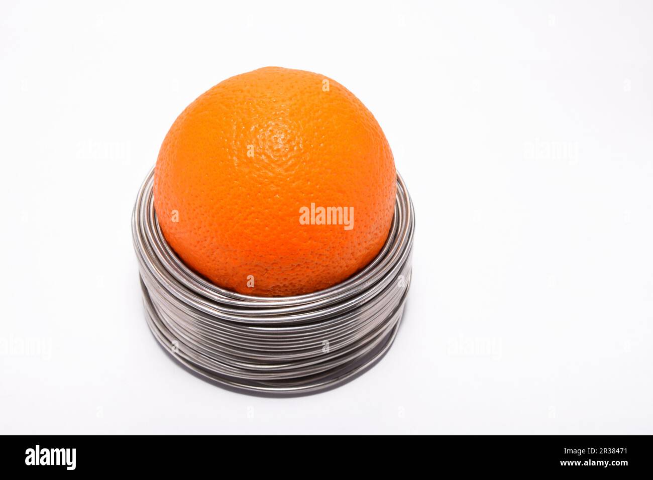 Wired orange: whole orange in coils of aluminium wire isolated on white ...
