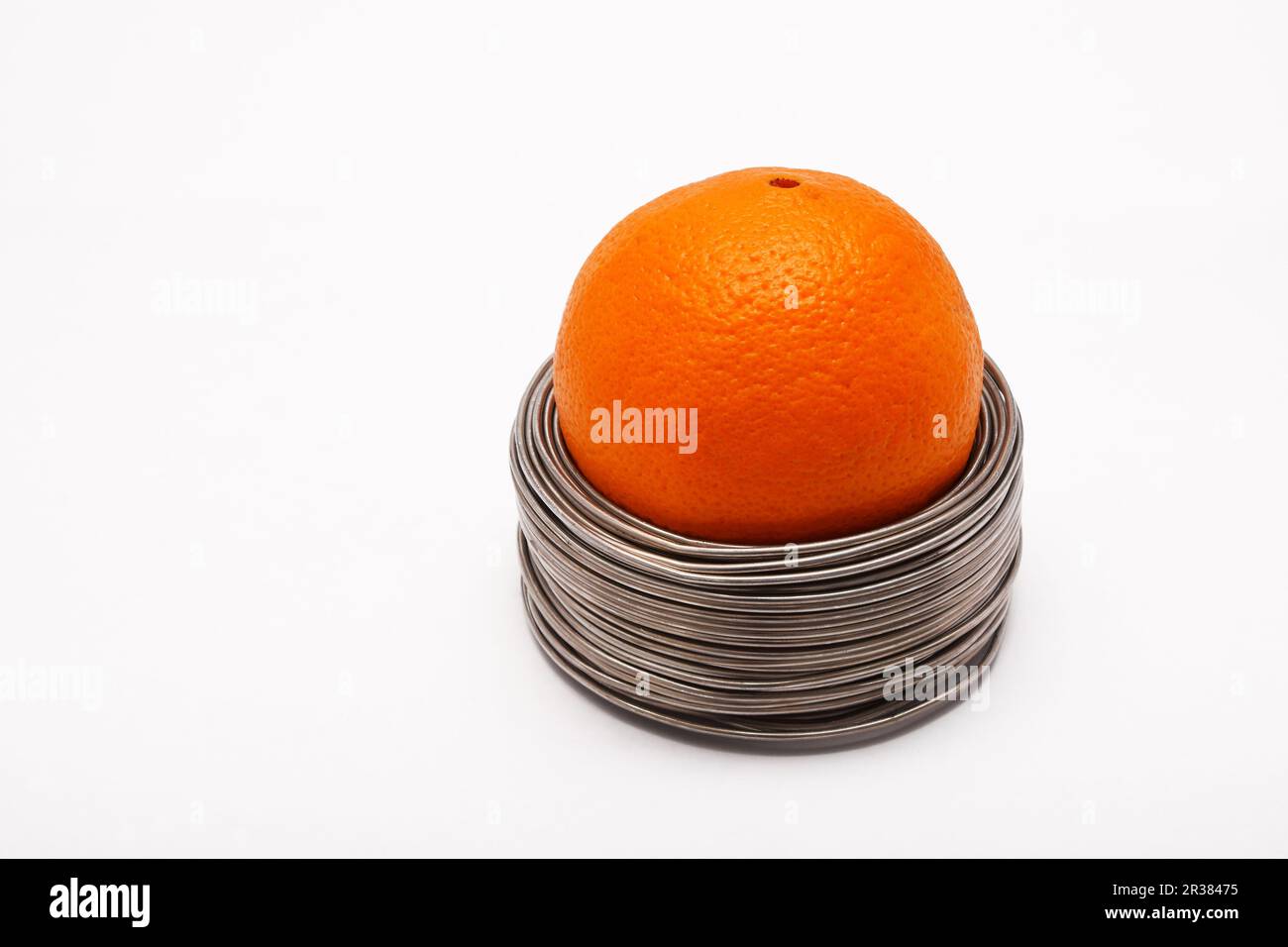 Wired orange: whole orange in coils of aluminium wire isolated on white ...