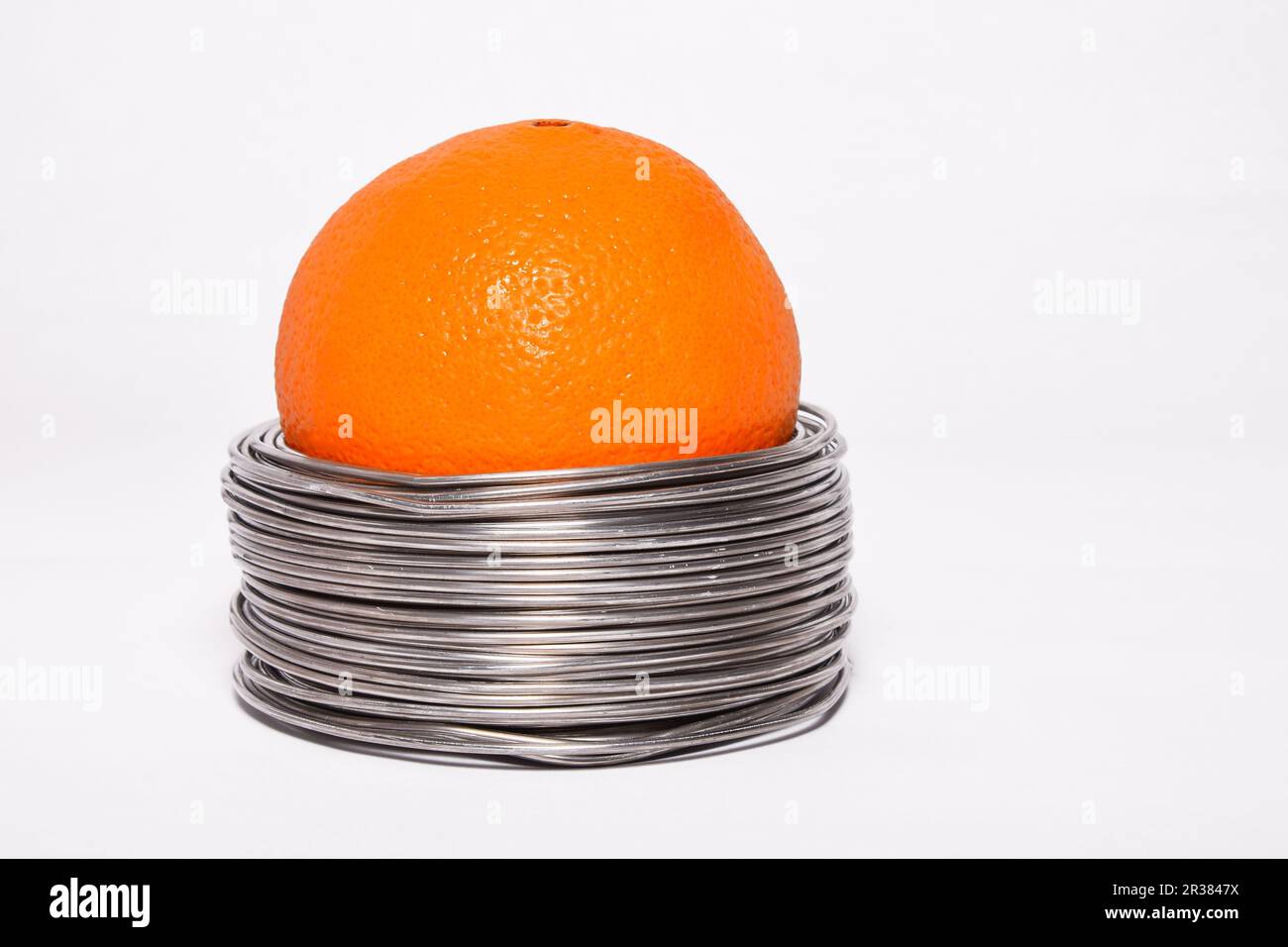 Wired orange: whole orange in coils of aluminium wire isolated on white ...
