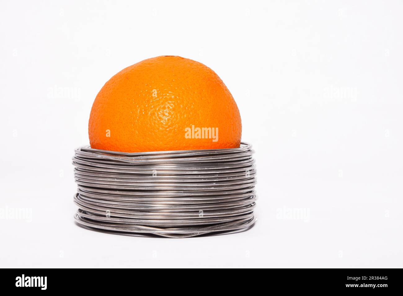 Wired orange: whole orange in coils of aluminium wire isolated on white ...