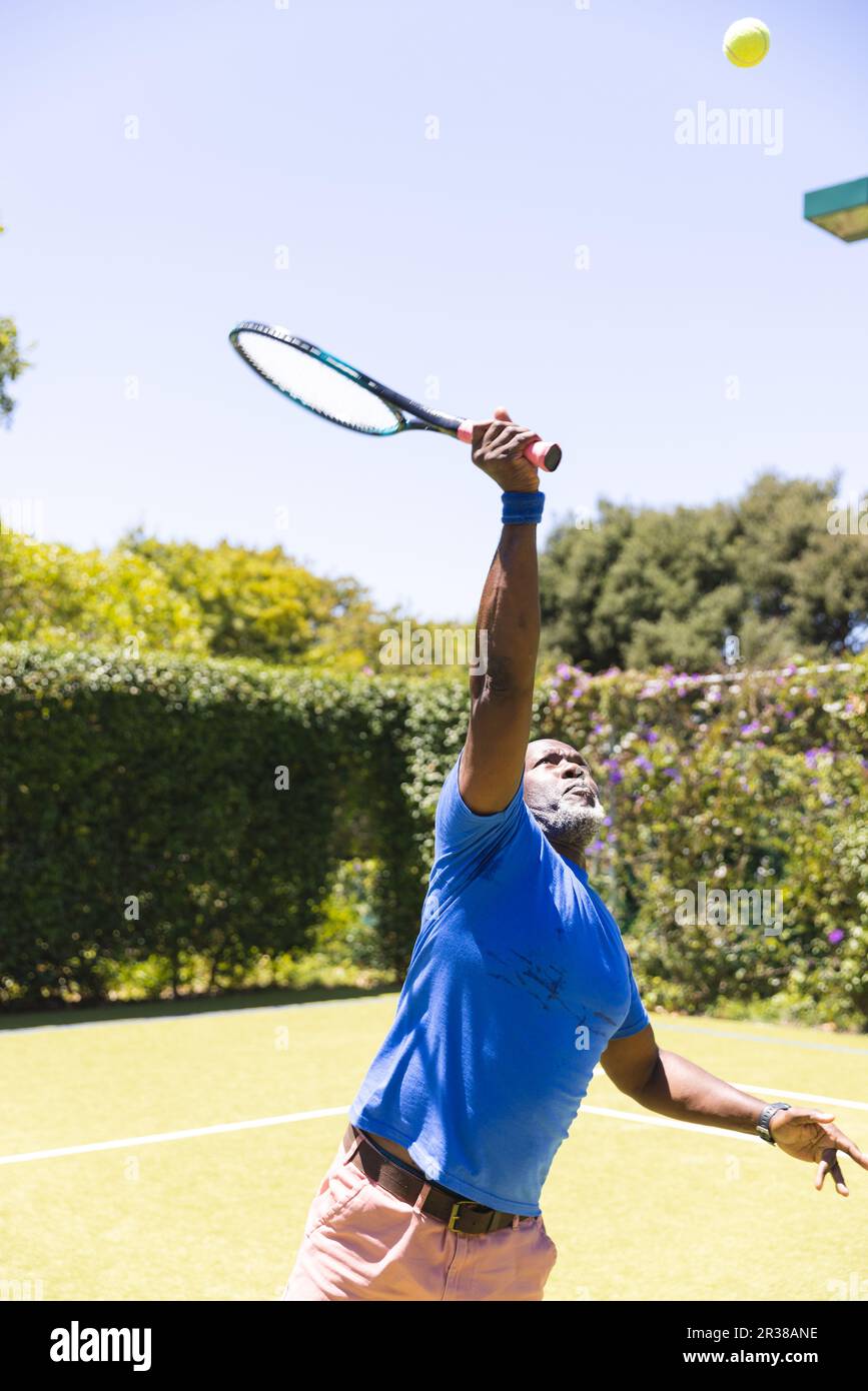 Happy senior african american man playing tennis stretching to hit high ...
