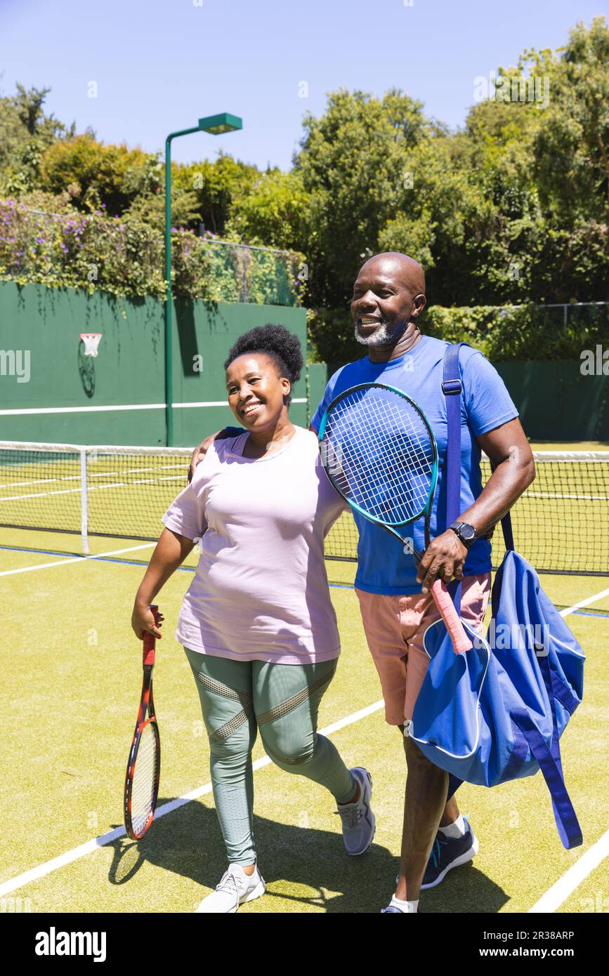 Happy senior african american couple walking with rackets on sunny ...