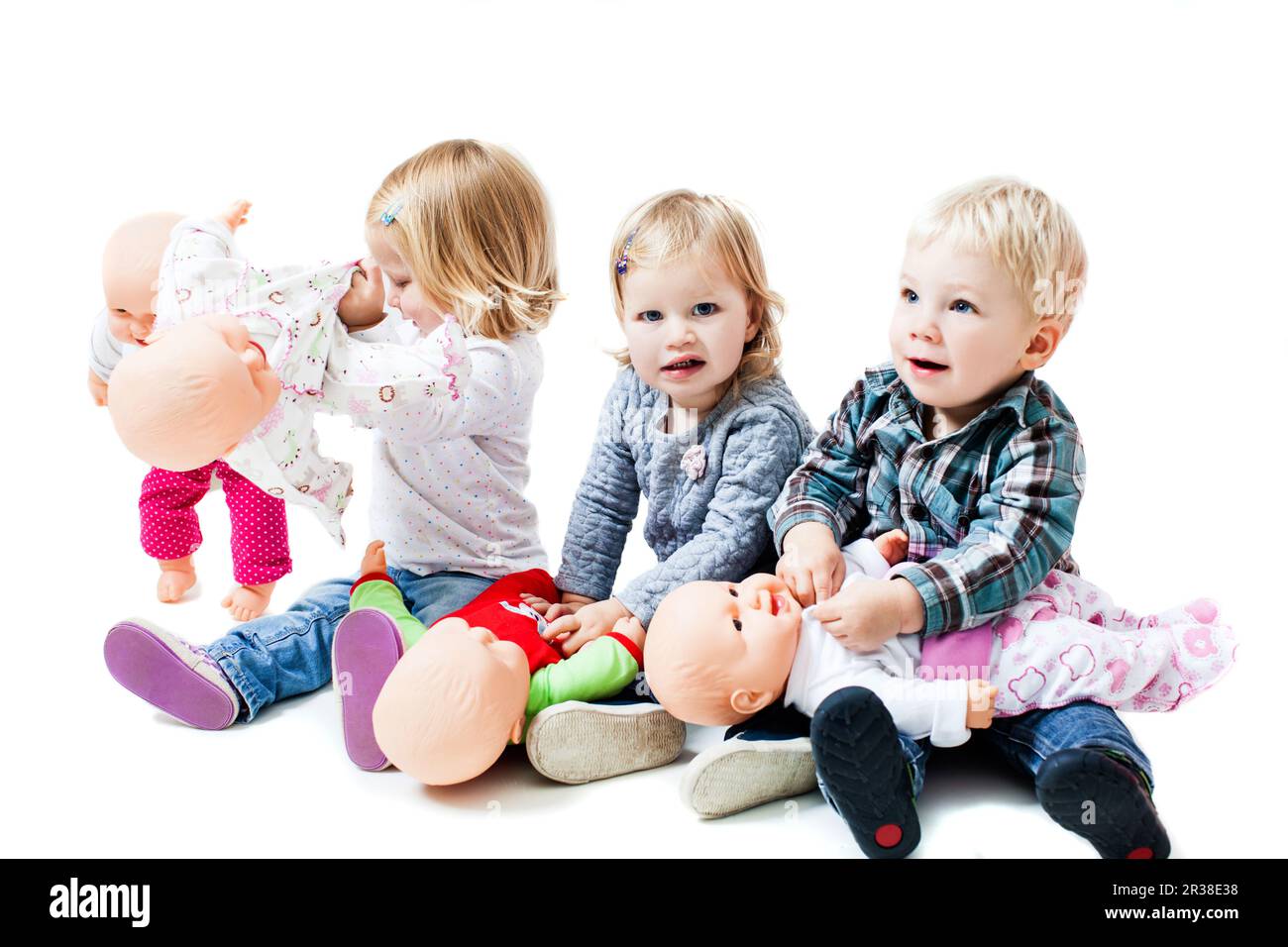 Kids playing with dolls. The boy and girls sit on a floor in the ...