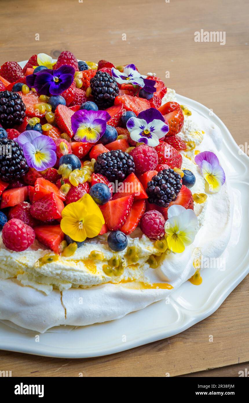 Pavlova with whipped cream, berries, passion fruit and edible flowers ...