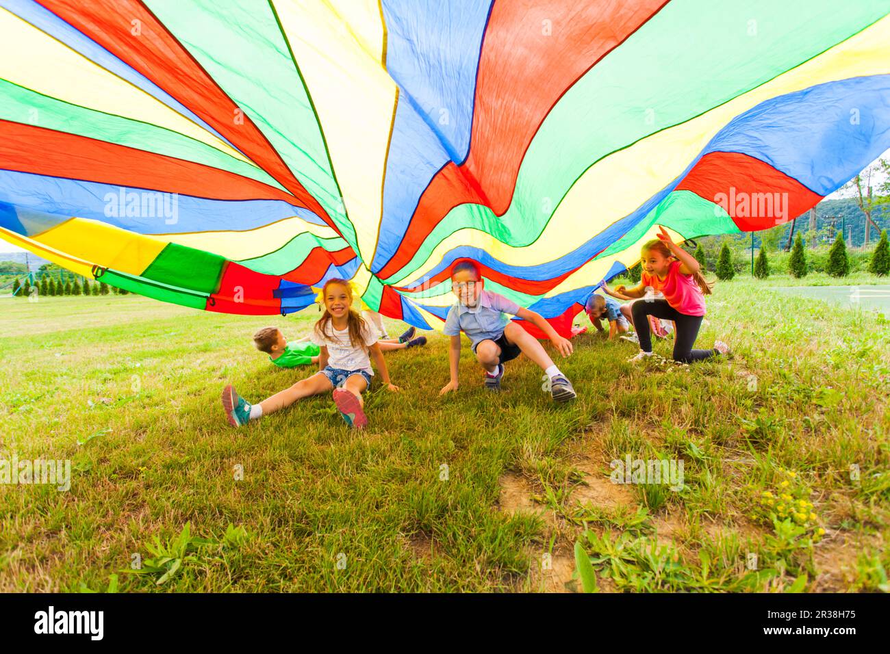Smiling boy and girl under colorful parachute Stock Photo - Alamy