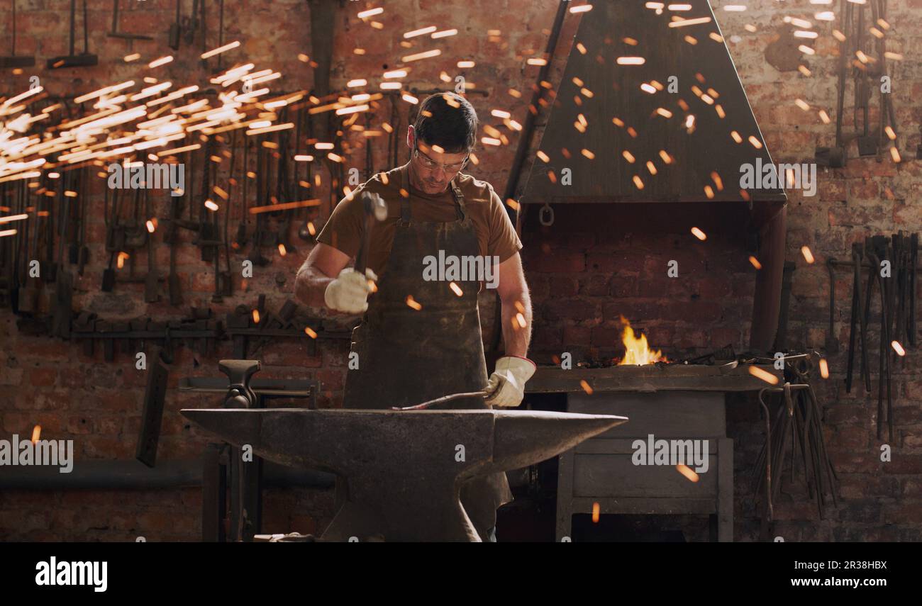 Hammer, anvil and fire with a man in a forge workshop for metal work ...
