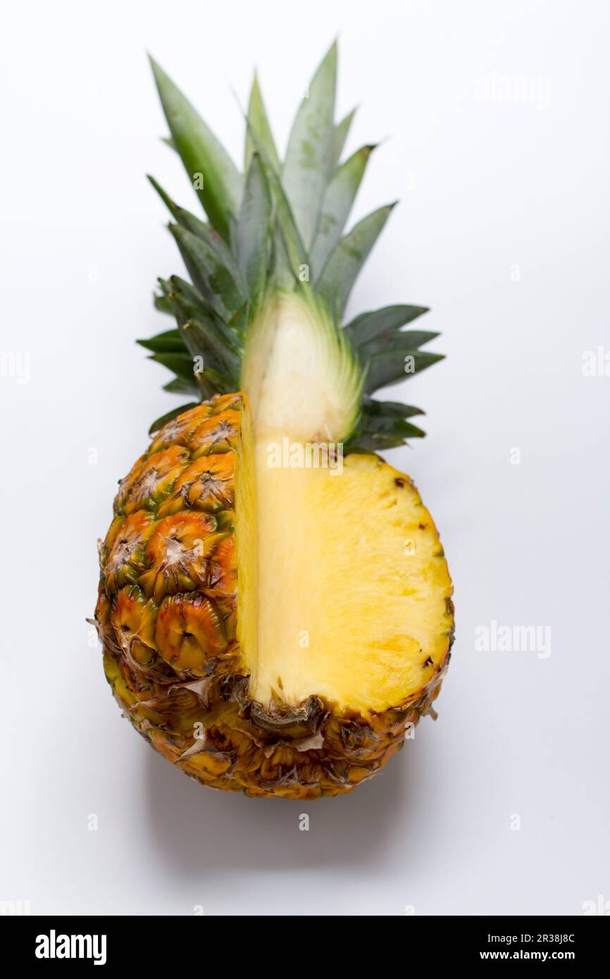 A pineapple on a white surface, with a quarter cut away Stock Photo - Alamy