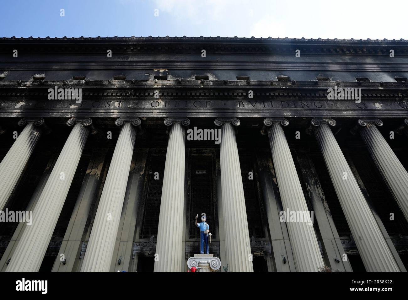 A statue of a postman stands in front of the burned Manila Post Office ...