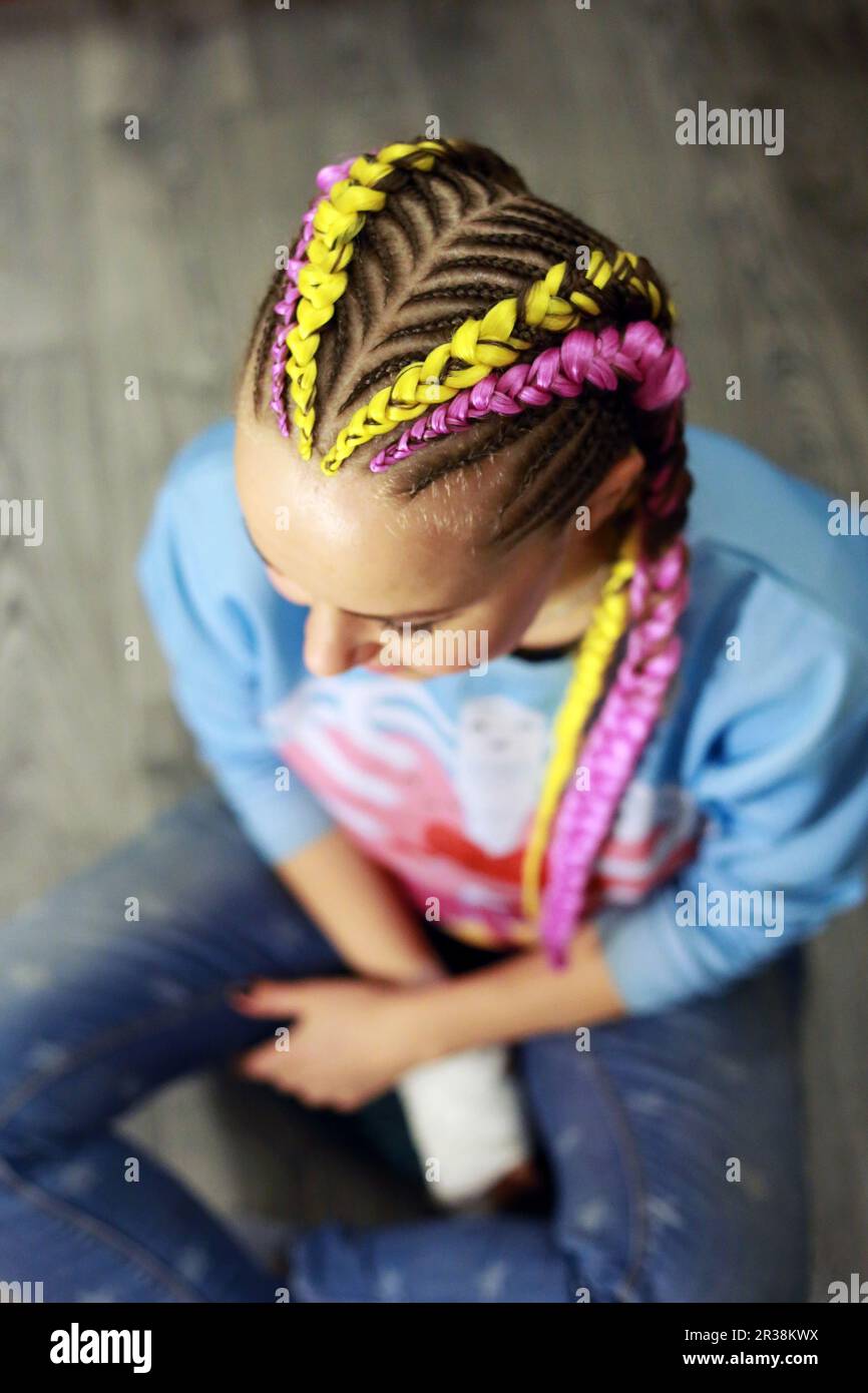 The girl stands with her back against a light background, thick braids ...