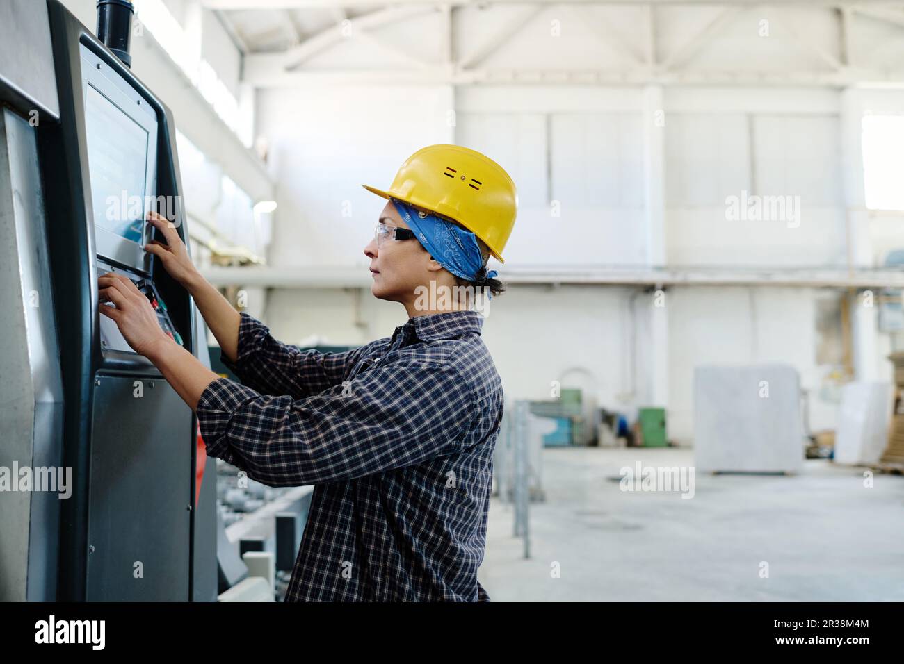 Female worker in hard hat pushing buttons on machine and looking at ...