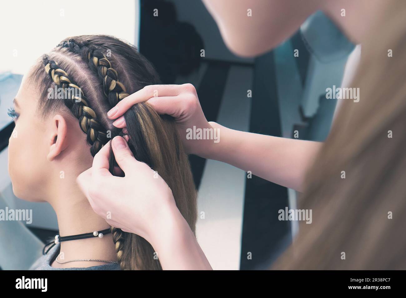 The master weaves braids on her head in a beauty salon close up, the ...