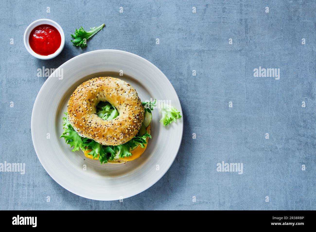 Ceramic plate with cheese sandwich on bagel with cucumber and lettuce ...
