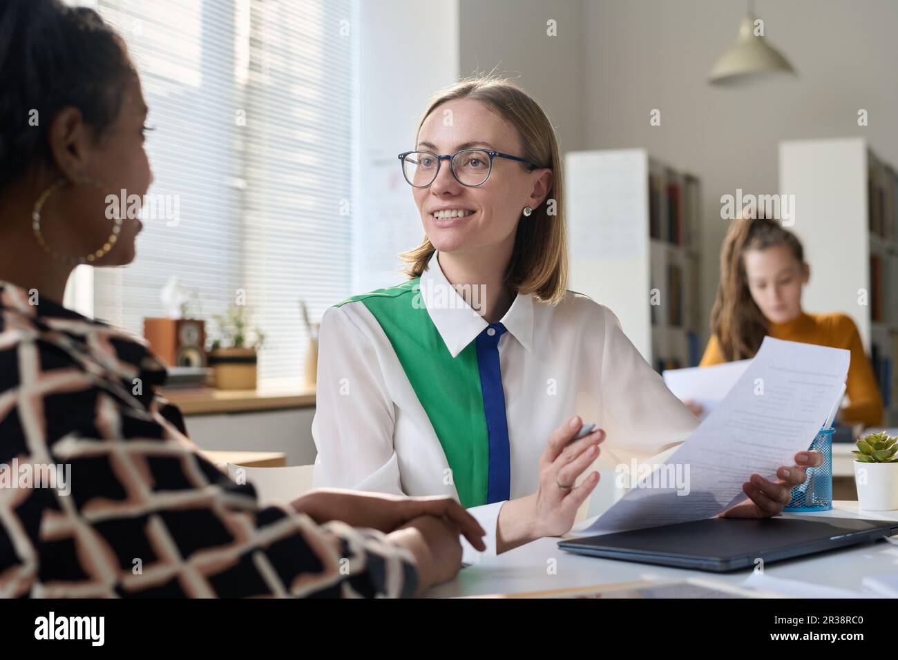 Young smiling teacher speaking English with student at table during ...