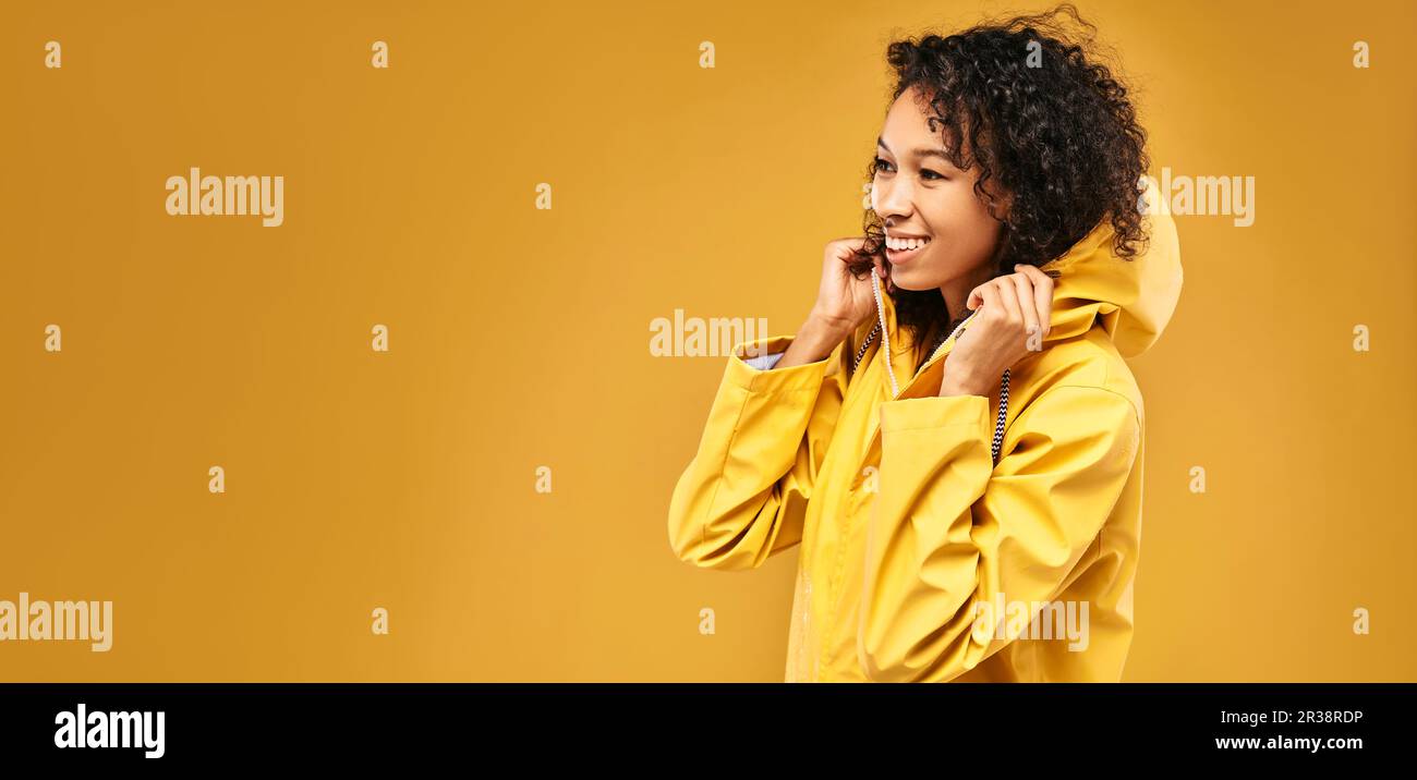 Portrait of positive African girl wearing raincoat with hood posing ...