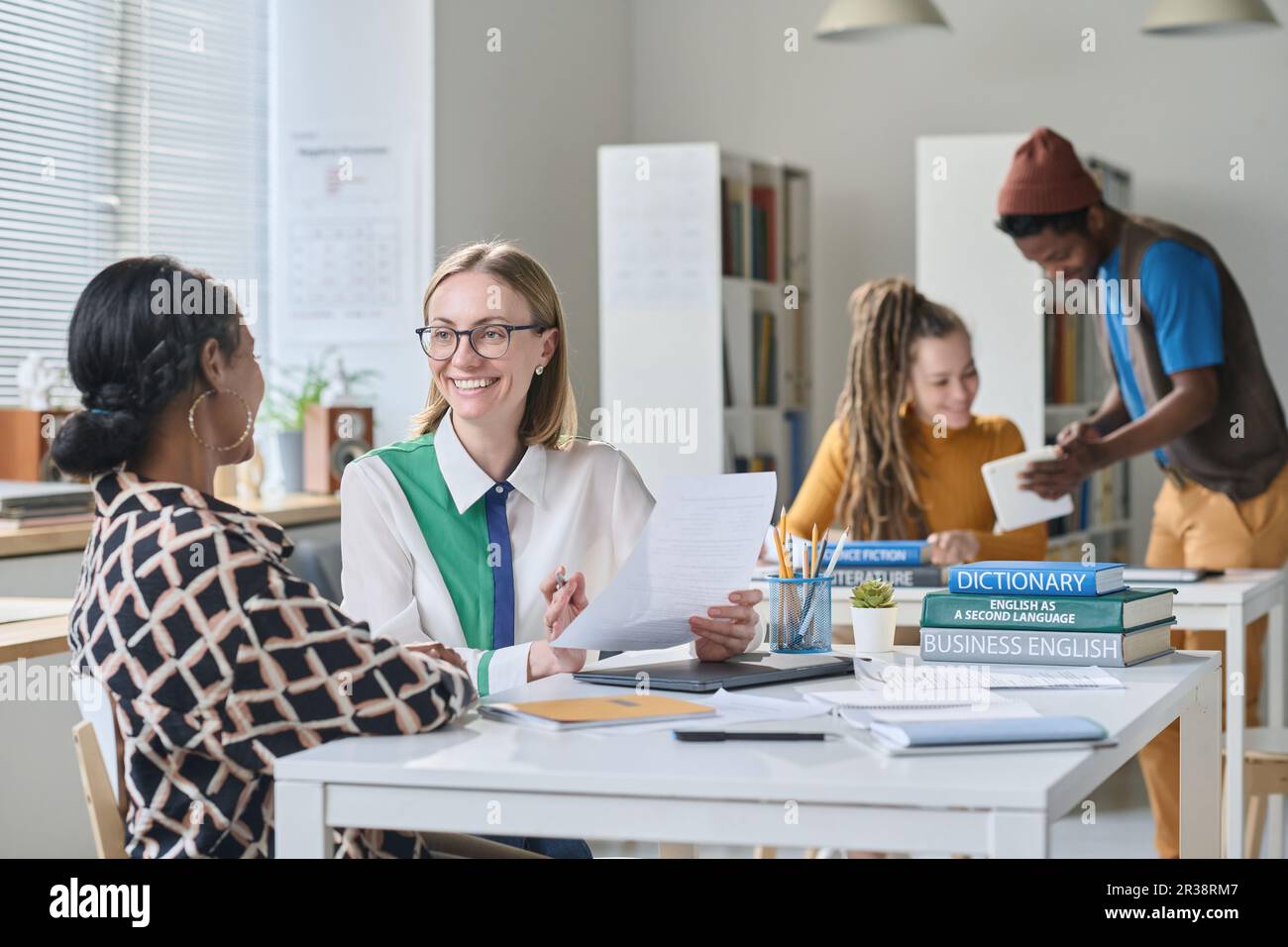 Smiling teacher speaking foreign language with student during lesson in ...