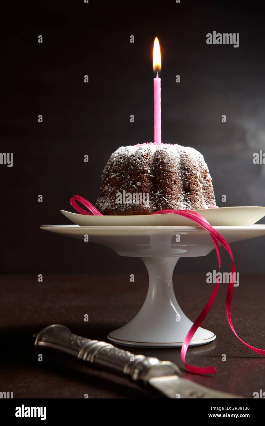 A mini chocolate cake with a candle on a cake stand Stock Photo - Alamy
