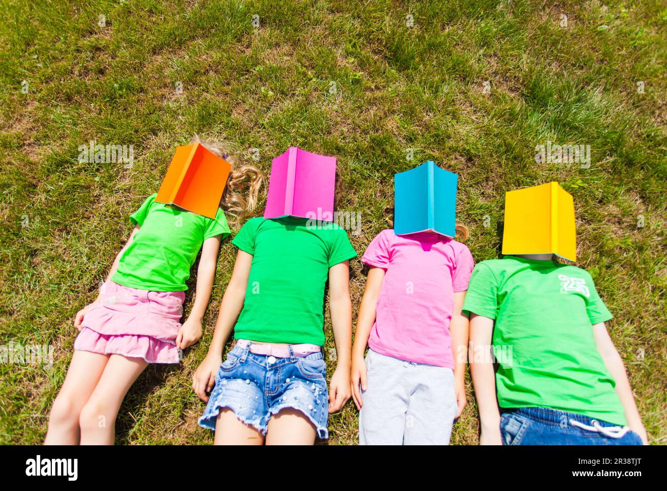 Four kids laying on a ground with books on their faces Stock Photo - Alamy