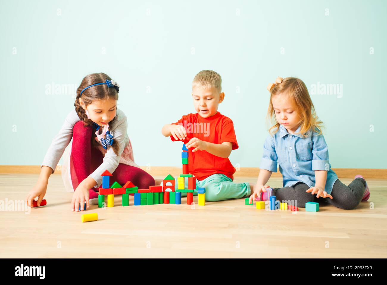 Three friends building with blocks on a floor Stock Photo - Alamy