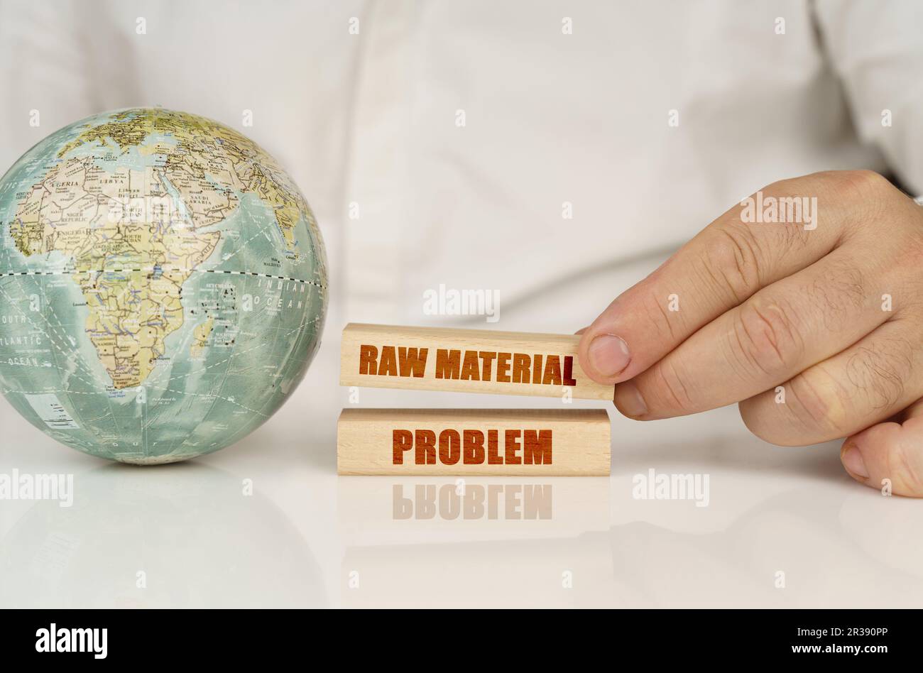 There is a globe on a white reflective surface, in the hands of wooden ...