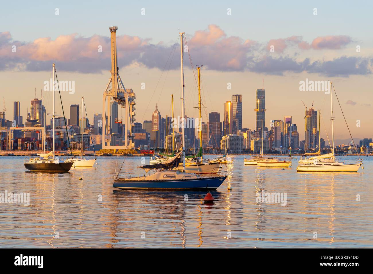 Yachts anchored on a calm coastal bay in front of cranes and city ...