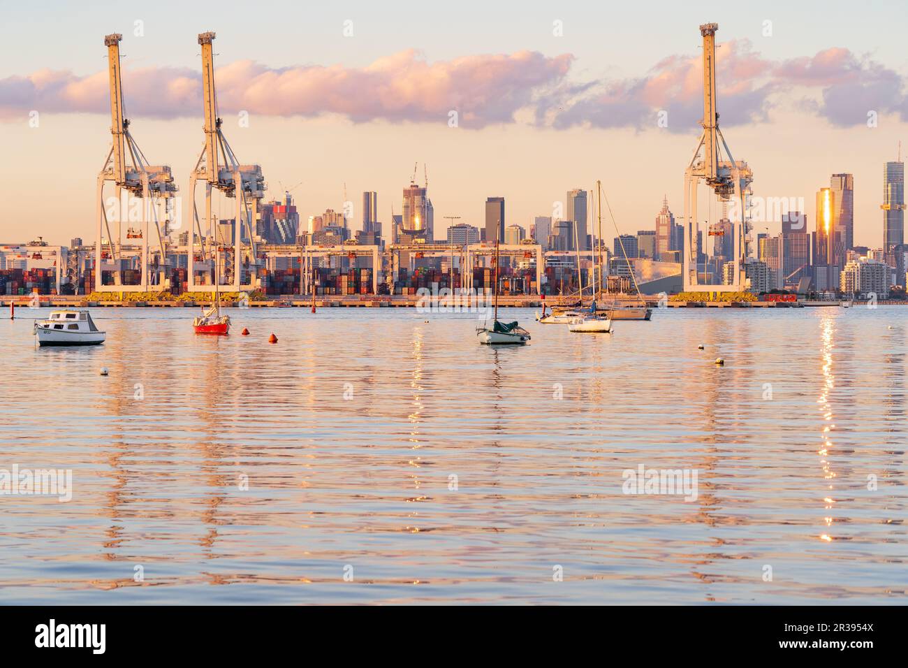 Small boats on a calm coastal bay in front of cranes and city buildings ...