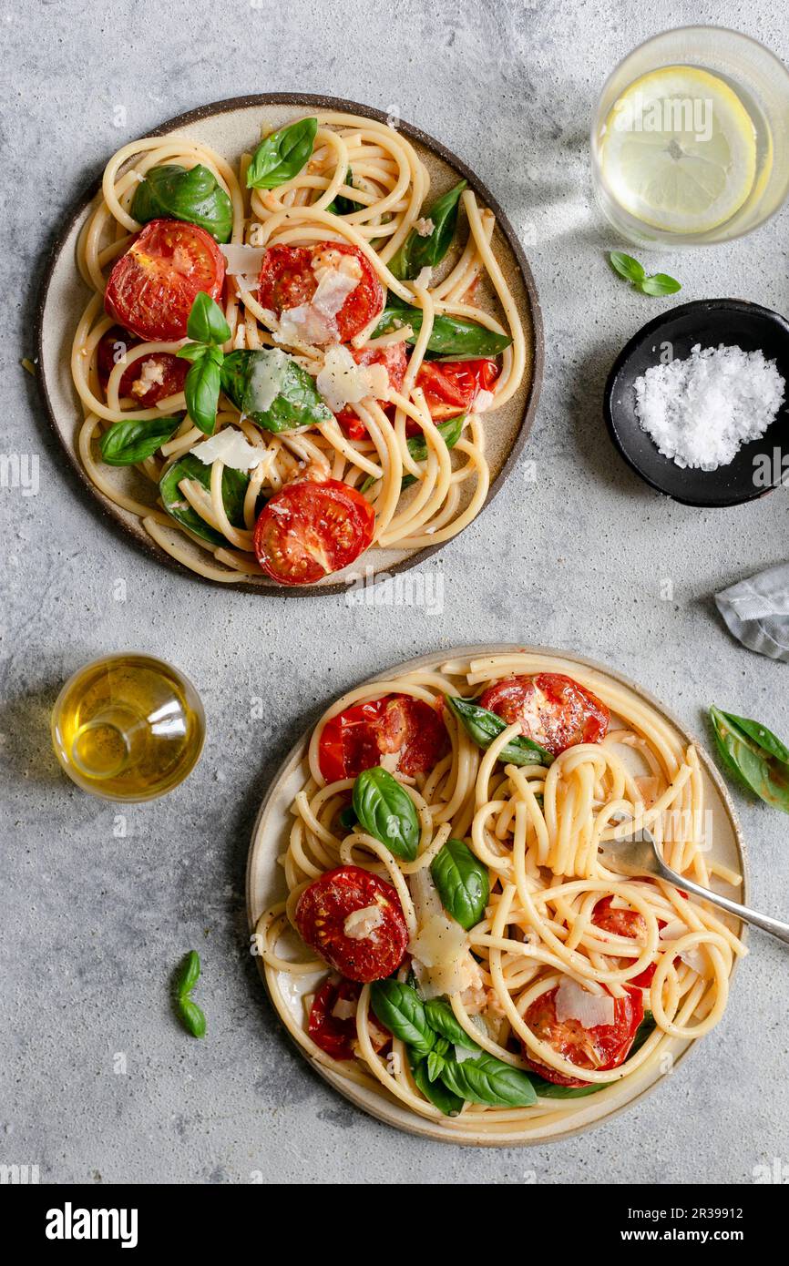 Two plates of bucatini pasta with roasted tomatoes and basil Stock ...