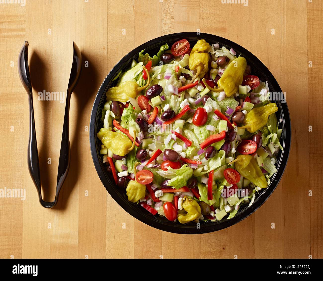 Greek Salad with Plastic Tongs shot on butcher block table from above ...