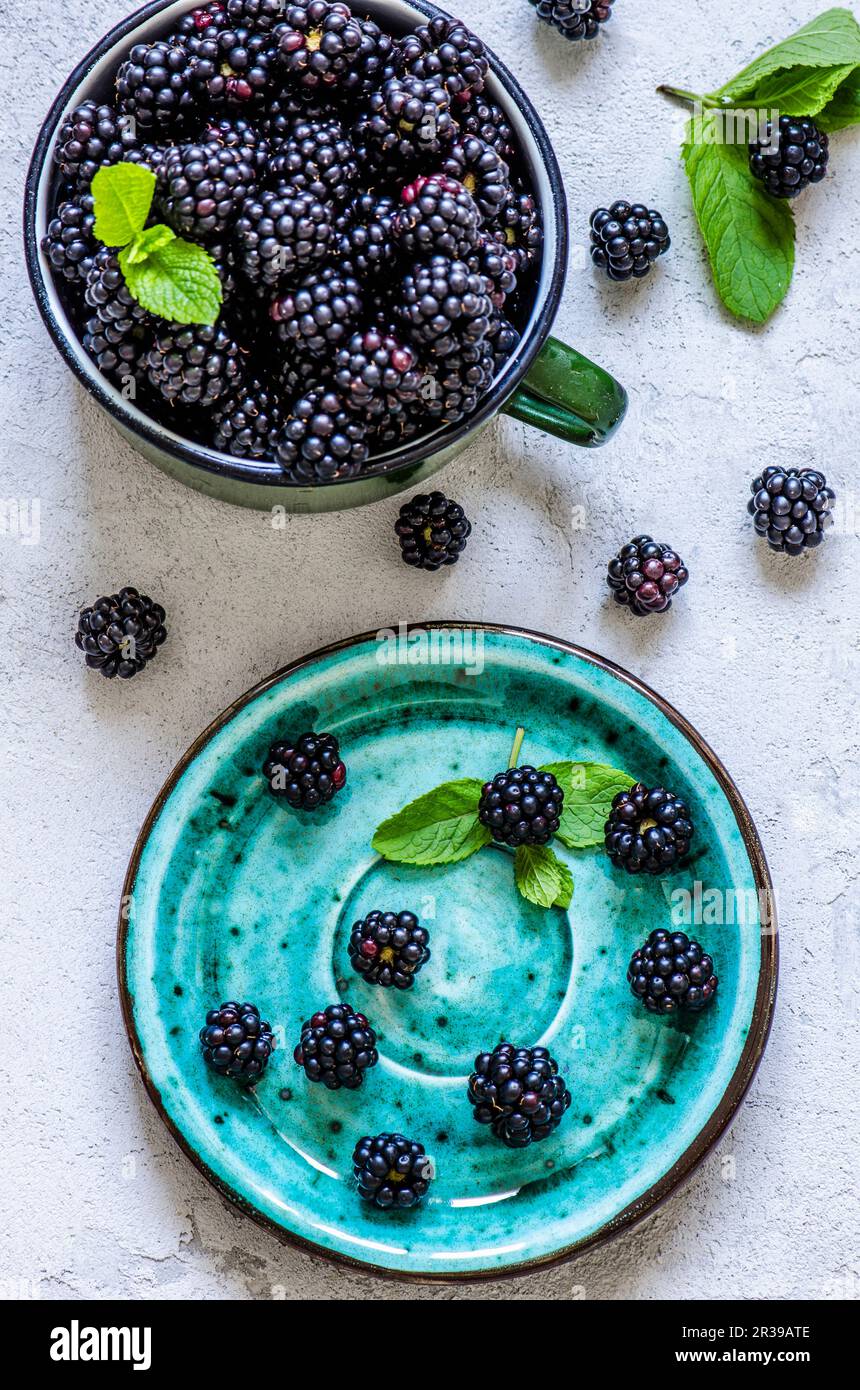 Blackberry harvest in an iron mug and a saucer on a concrete background ...