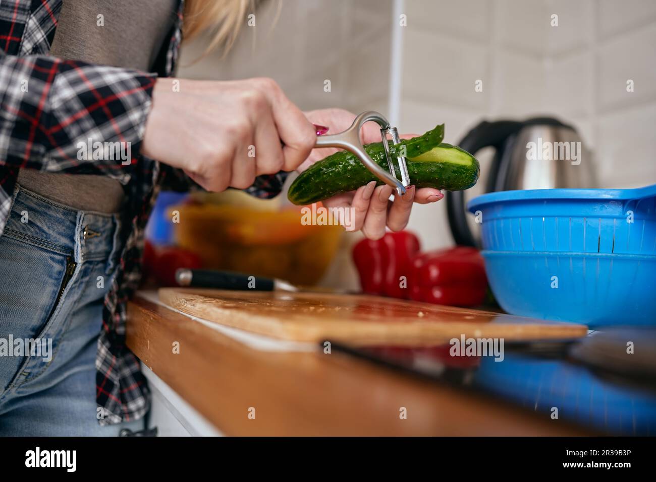 Female person peeling off a cucumber skin with a peeler tool. Housewife ...