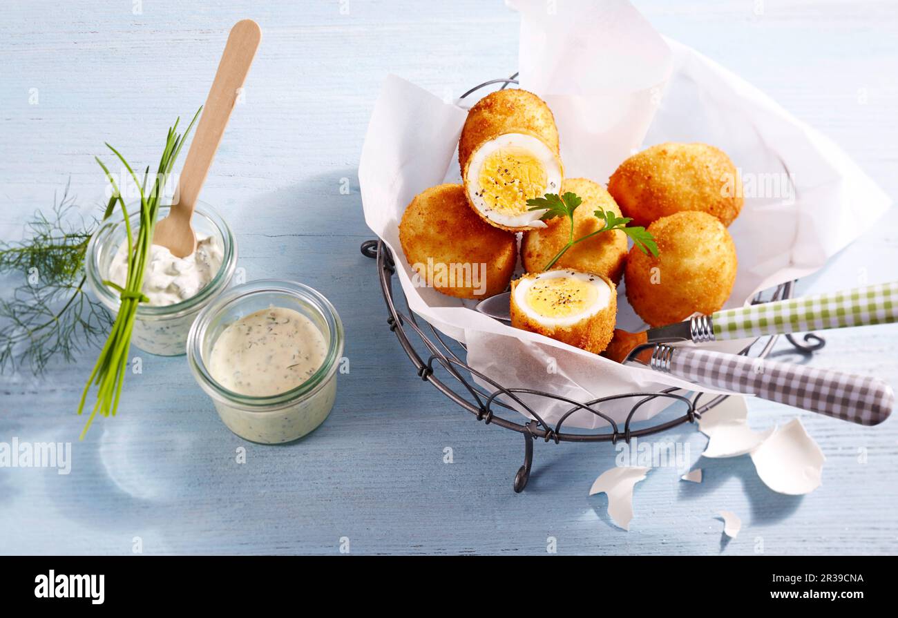 Breaded eggs in parchment paper in a metal basket next to a mustard dip ...
