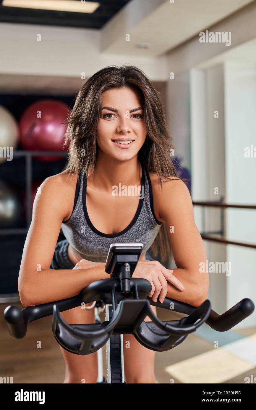 Muscular young woman working out on the exercise bike at the gym ...