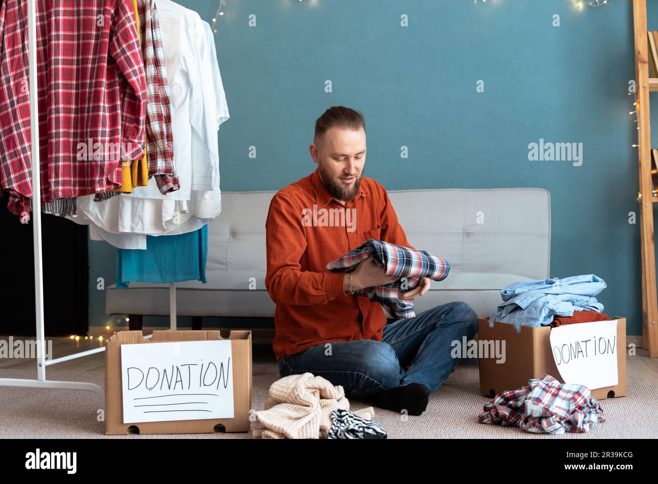 Man folding old clothes in donation box sitting on the floor at home ...