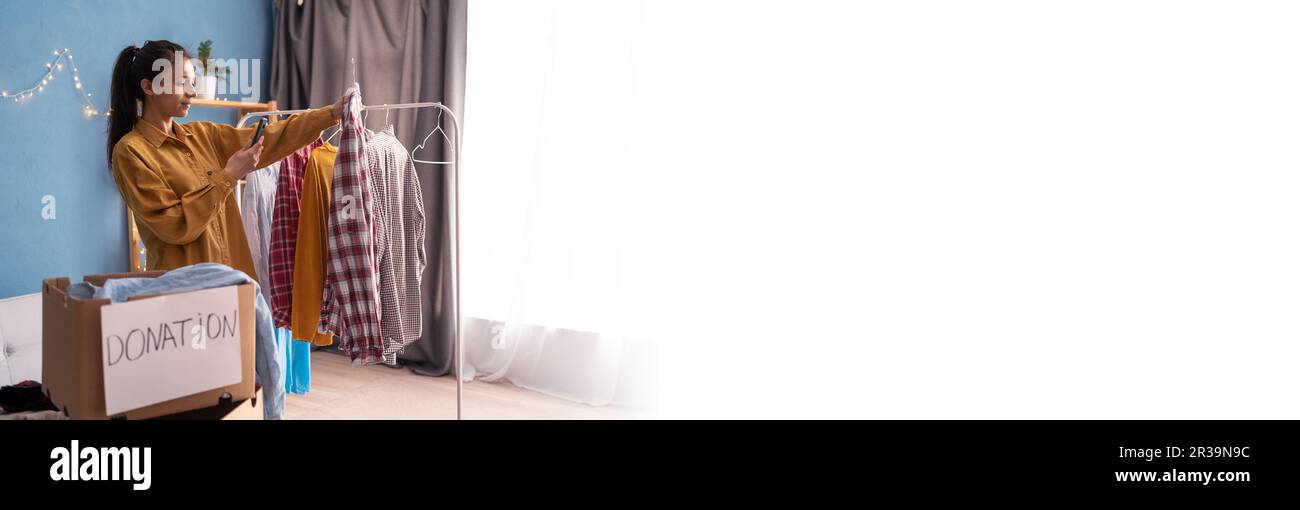 Young woman choosing clothes for donation at home taking photo of shirt ...