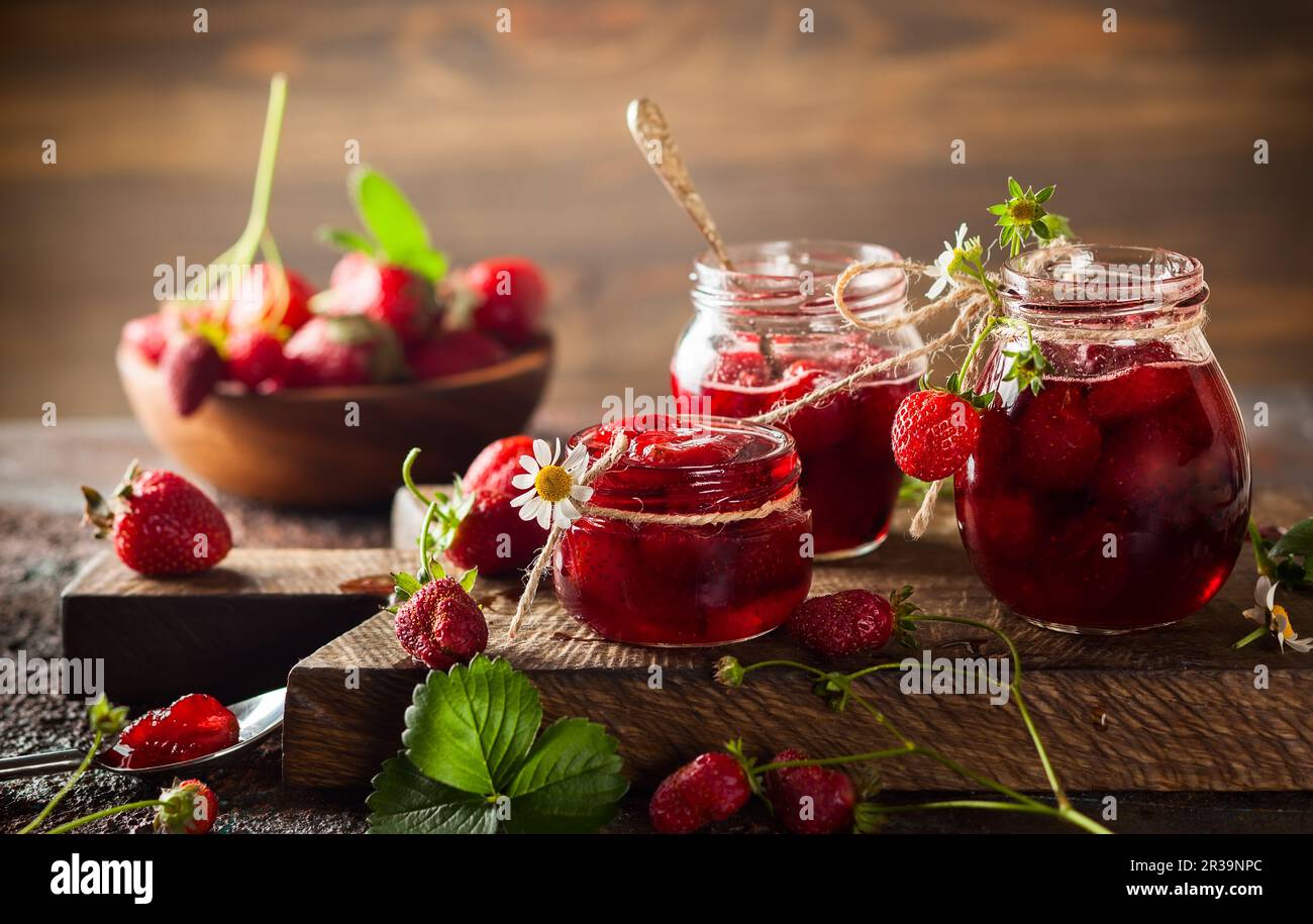 Homemade strawberry jam in glass jars on wooden board in rustic style ...