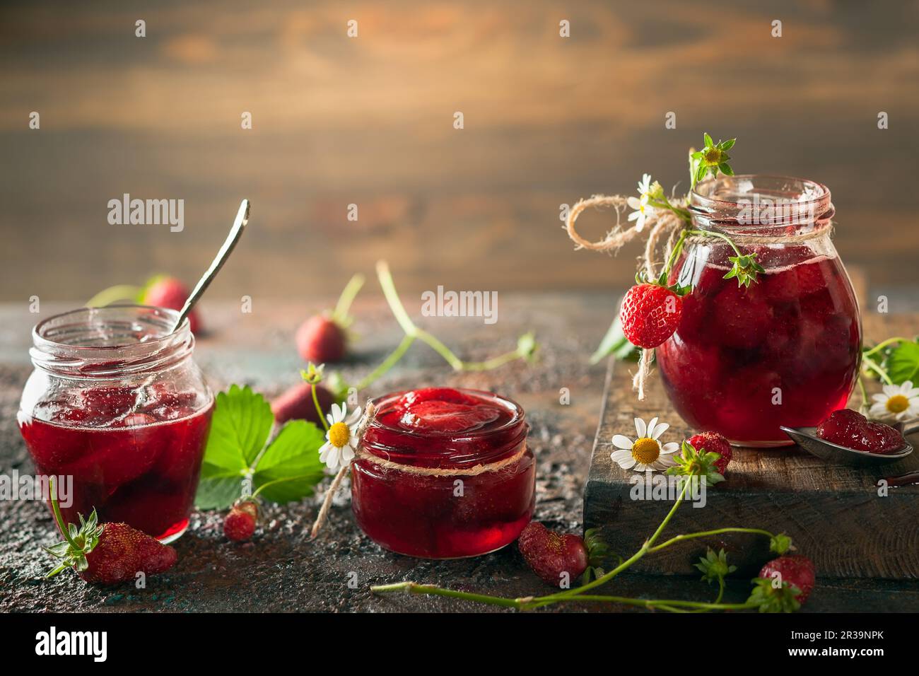 Homemade strawberry jam in glass jars on wooden board in rustic style ...